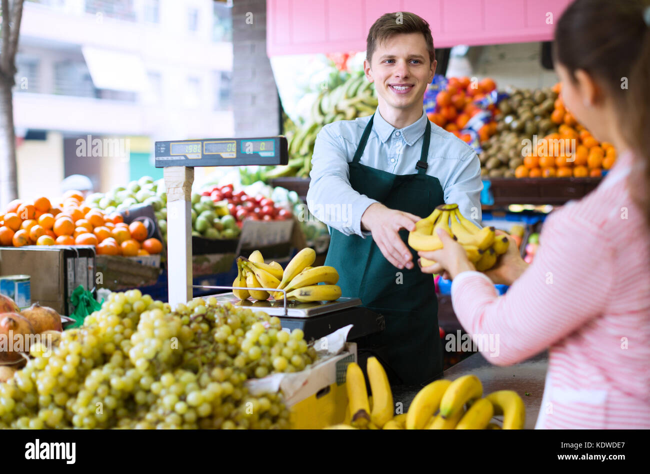 Friendly seller weighing healthy bananas on scale for young woman Stock ...