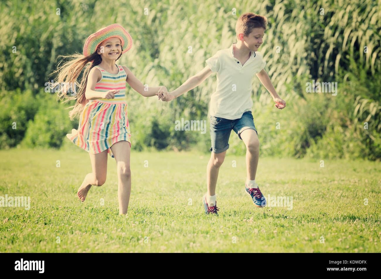 Two happy joyful school children running together holding hands in park ...