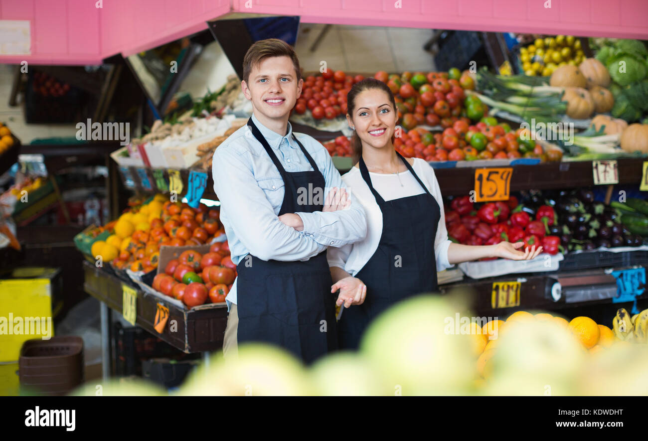 Friendly young happy sellers having vegetables and fruits on displays ...