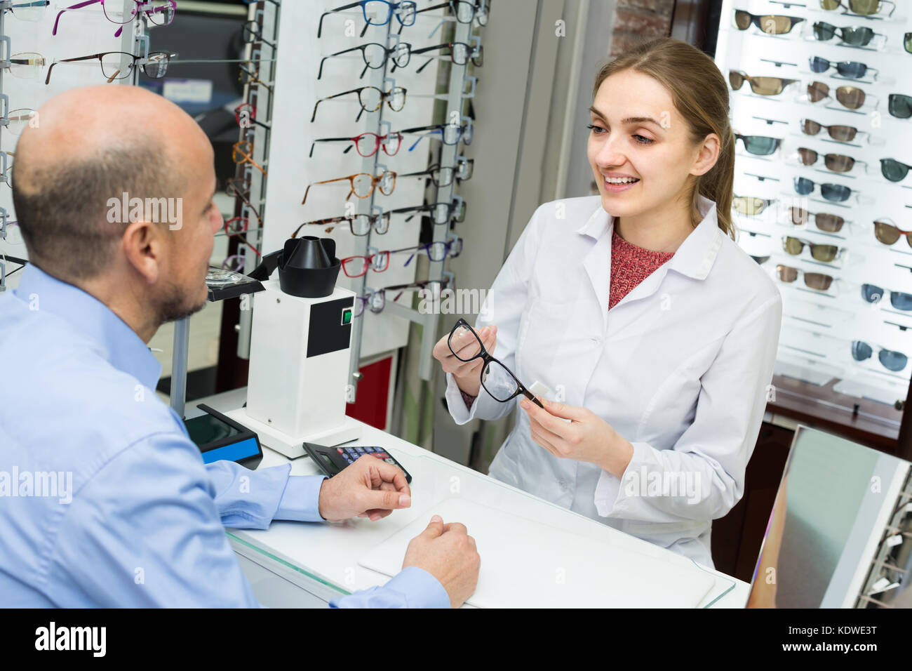 Female optician offering glasses frames to male customer and smiling ...