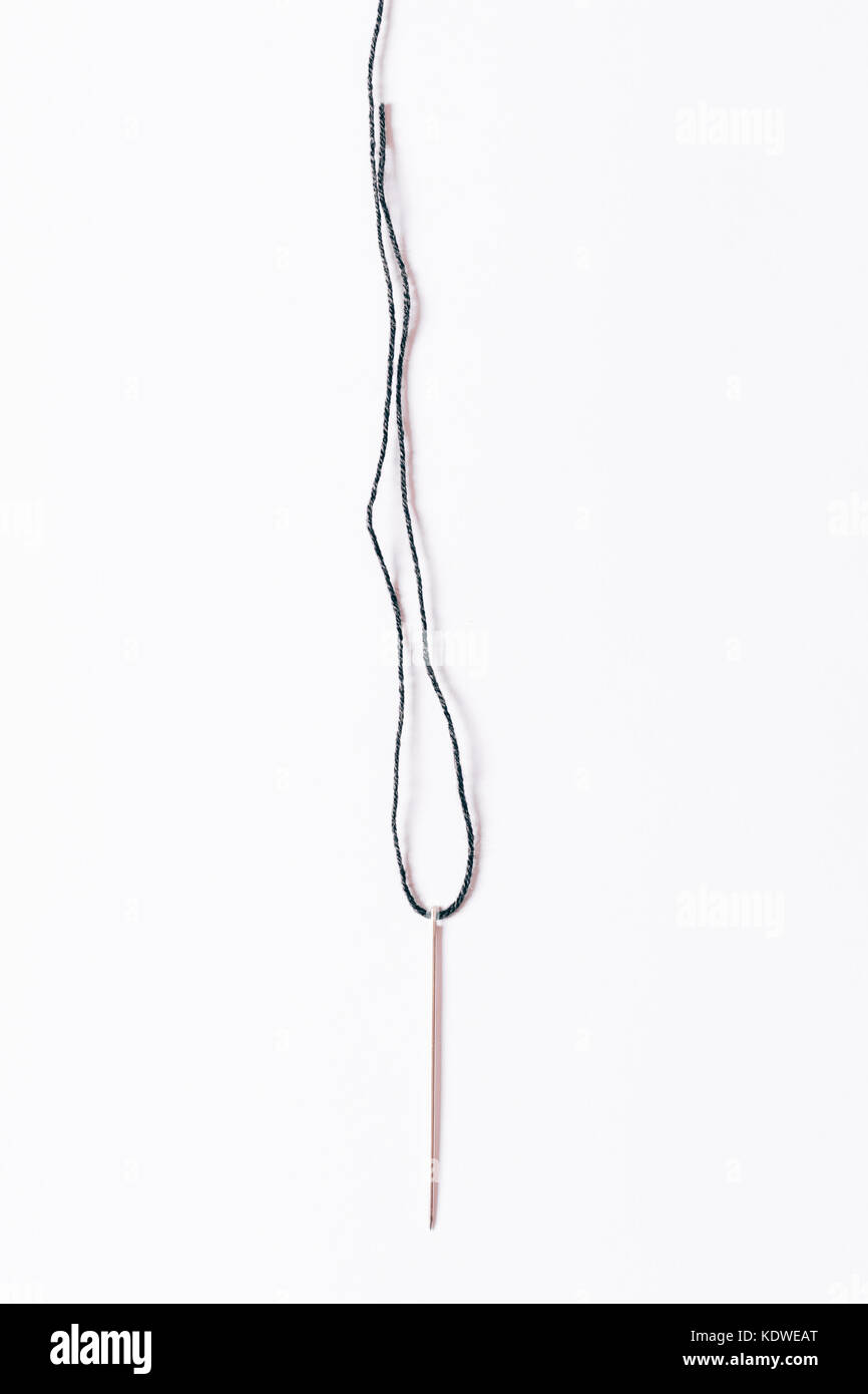 Vertical image of a needle with a thread on a white table top view ...