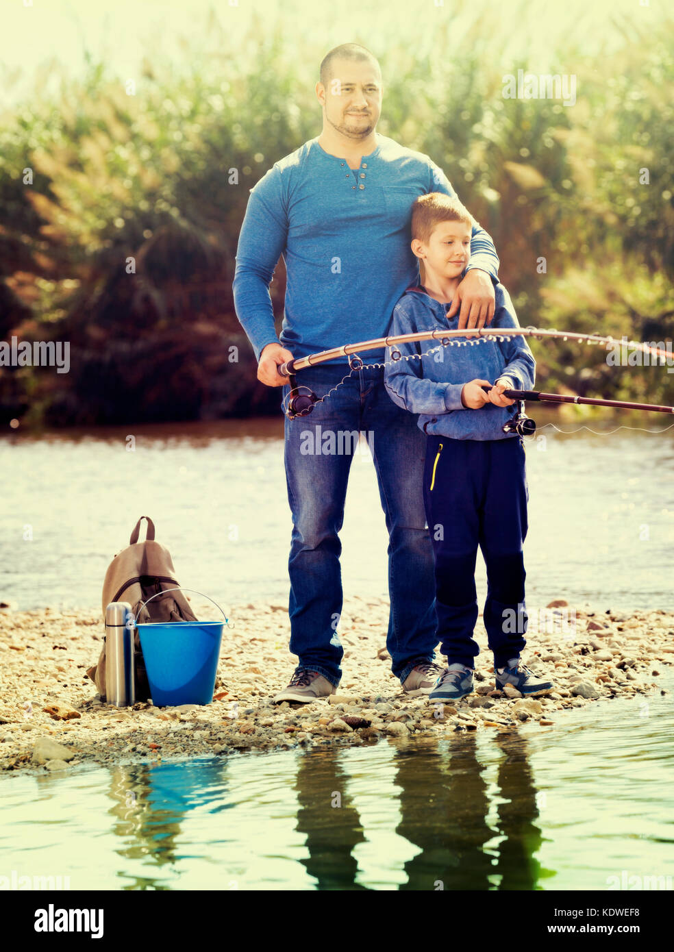 Portrait of glad father and cute son fishing with rods in summer day ...