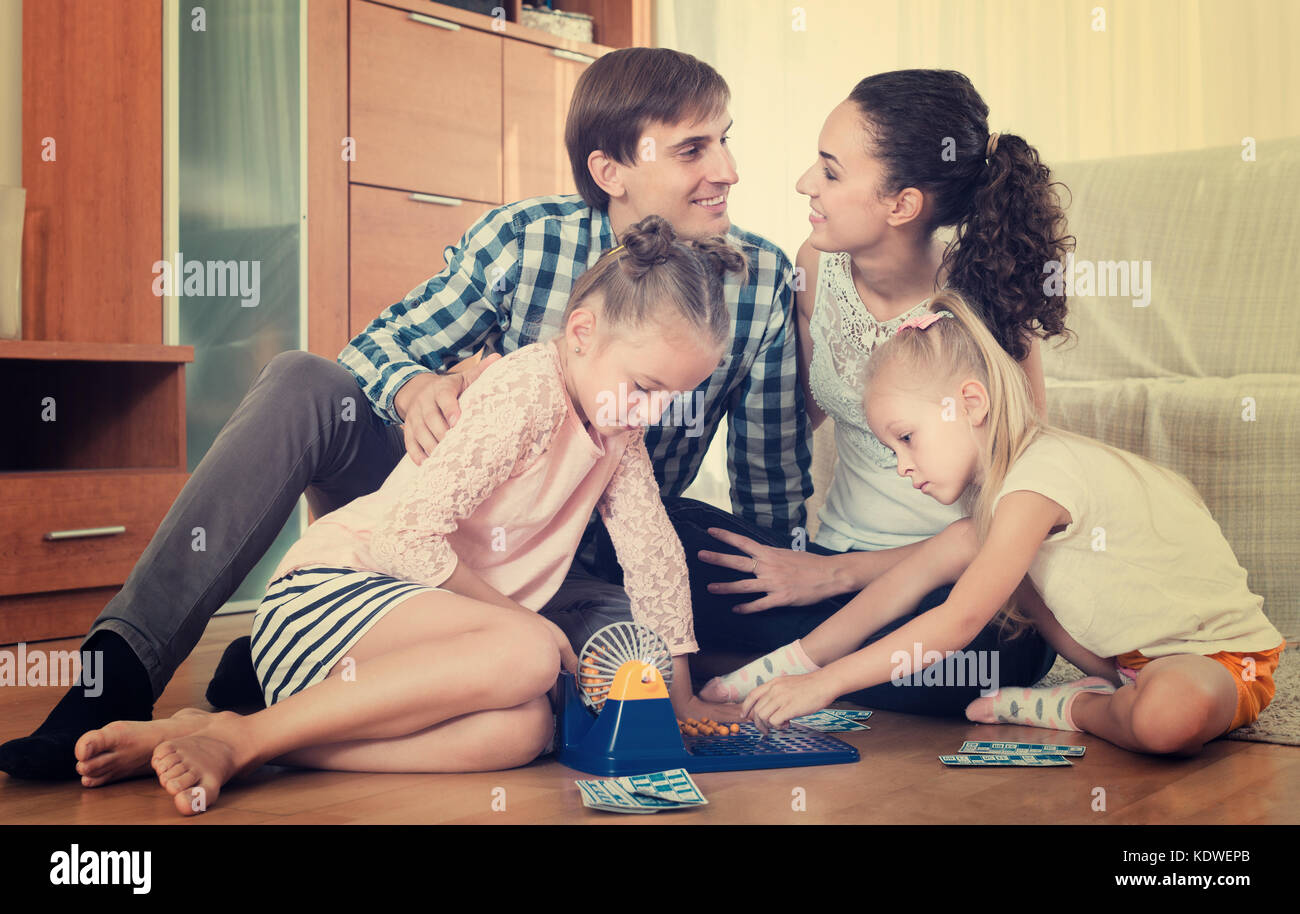 Happy young parents with two little daughters playing at lotto at home ...