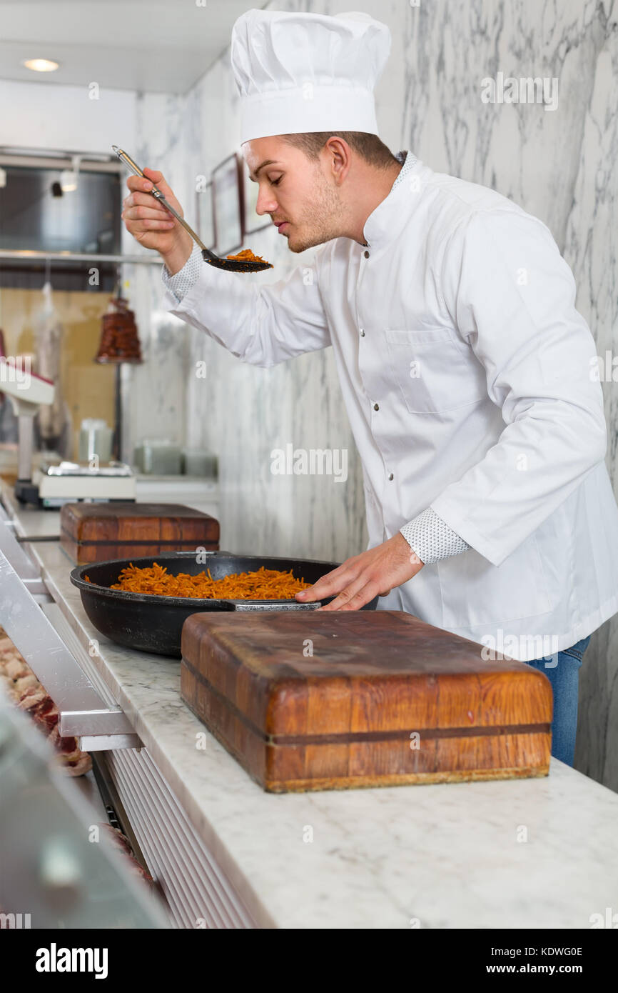 Smiling chief in professional clothing cooking fresh meat Stock Photo ...