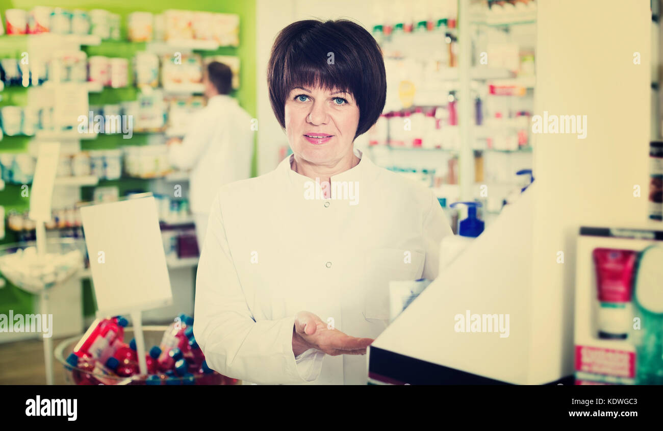 Smiling woman druggist wearing white coat standing among shelves in ...