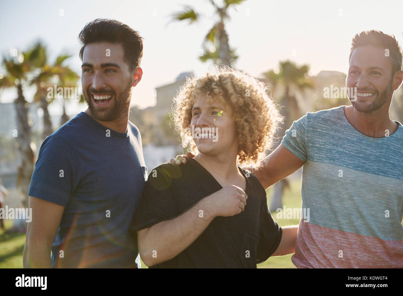 Portrait of three happy men standing outside together looking away ...