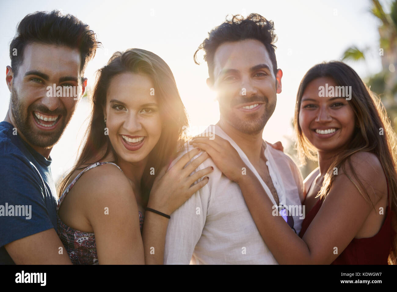 Portrait of four happy friends standing together outside in sunlight ...