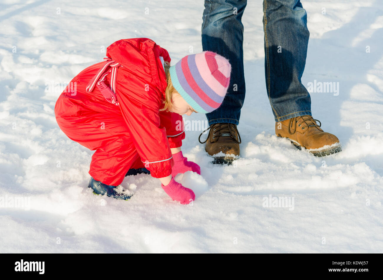 Cute toddler kid playing in the snow. Little girl child crouching down ...