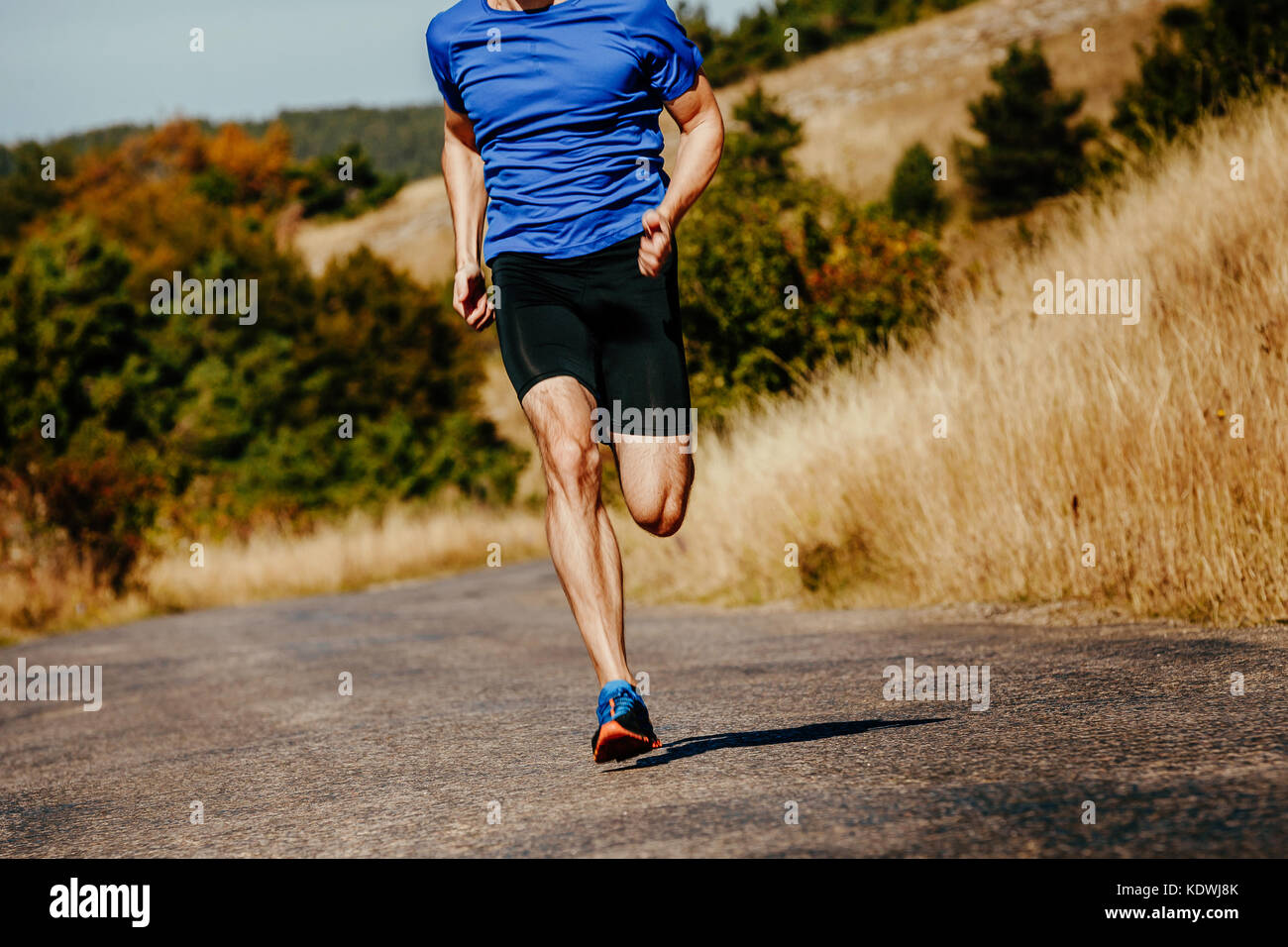 muscular athlete men runner running on asphalt road in autumn field ...