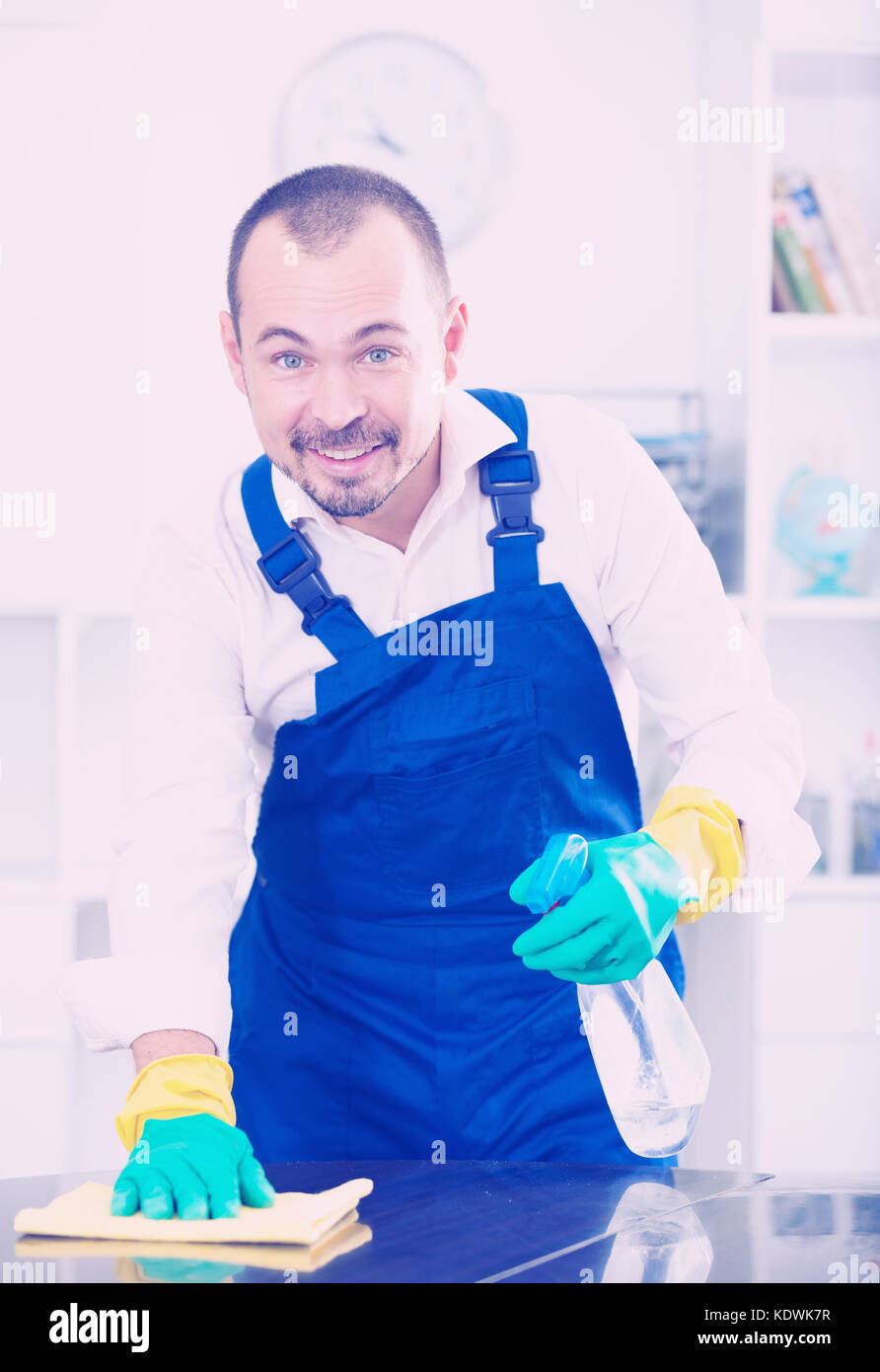 Positive young man in apron cleaning his office desk by cleanser Stock ...