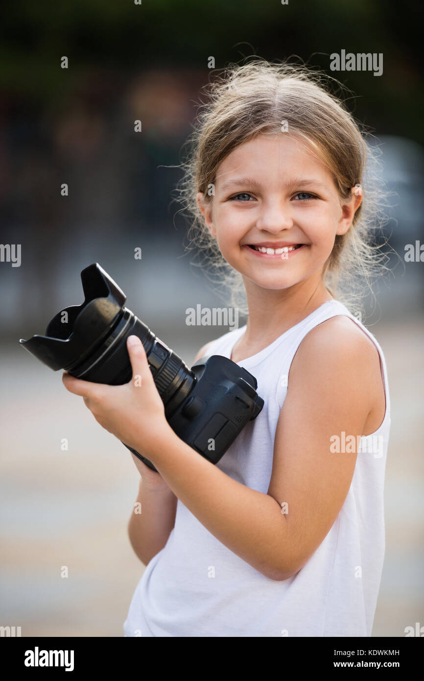 Smiling diligent girl taking pictures with professional camera outdoors ...