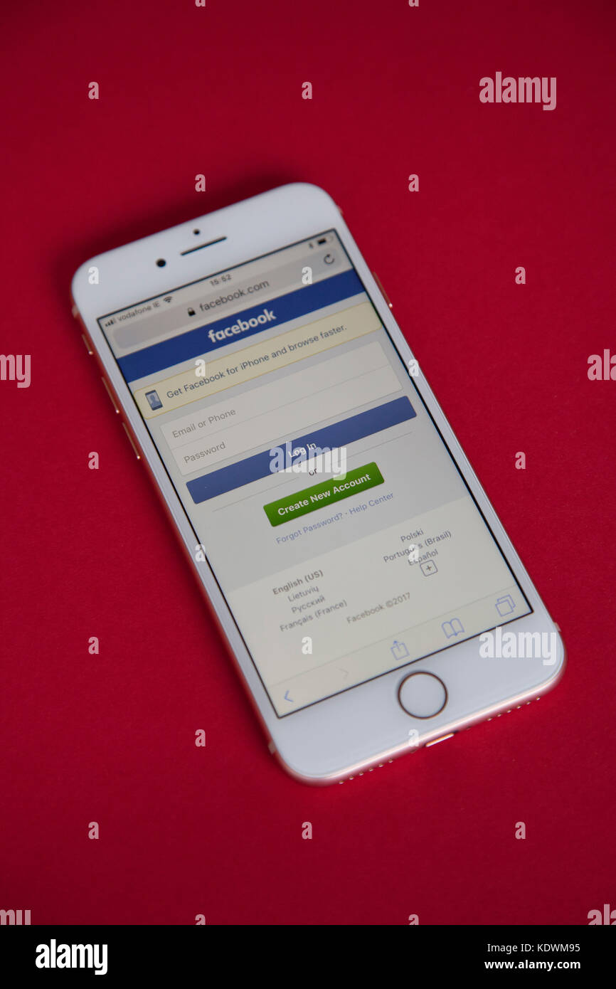 Apple iPhone 8 model with Facebook login screen against a red colour ...