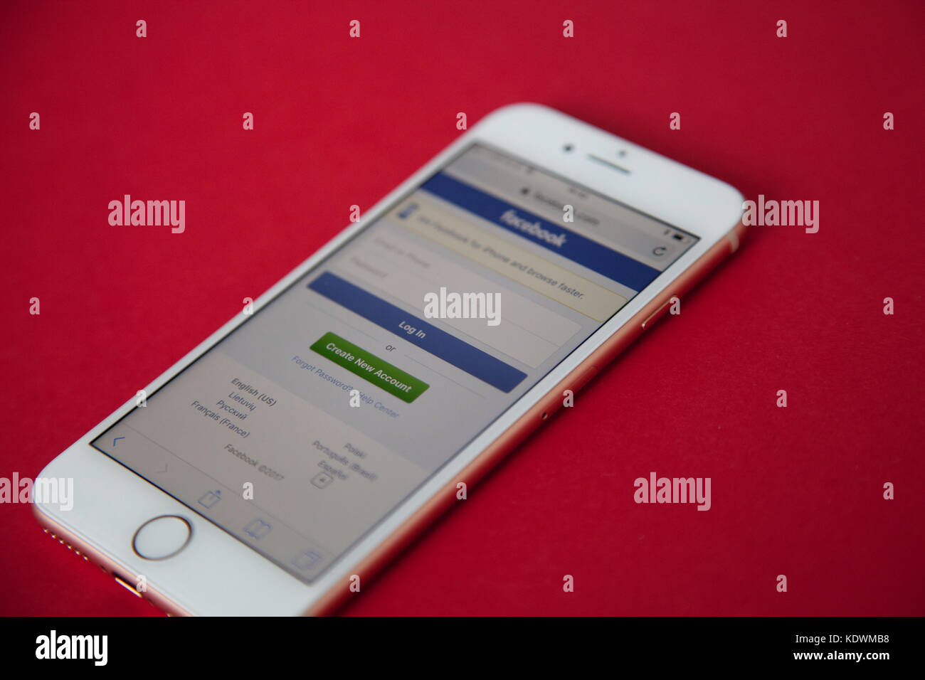 Apple iPhone 8 model with Facebook login screen against a red colour ...