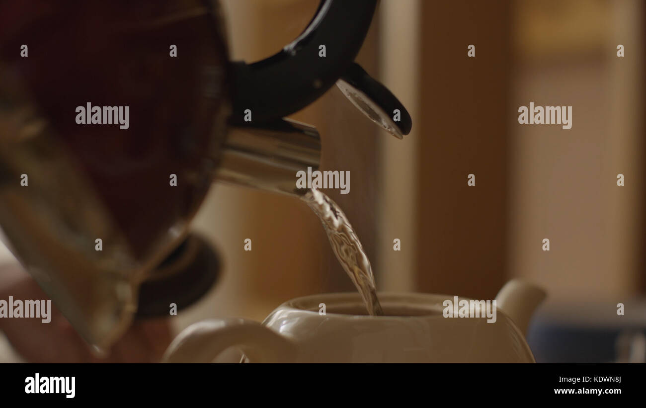 Woman pours boiling water into the cup and brew tea in a tea bag. The ...