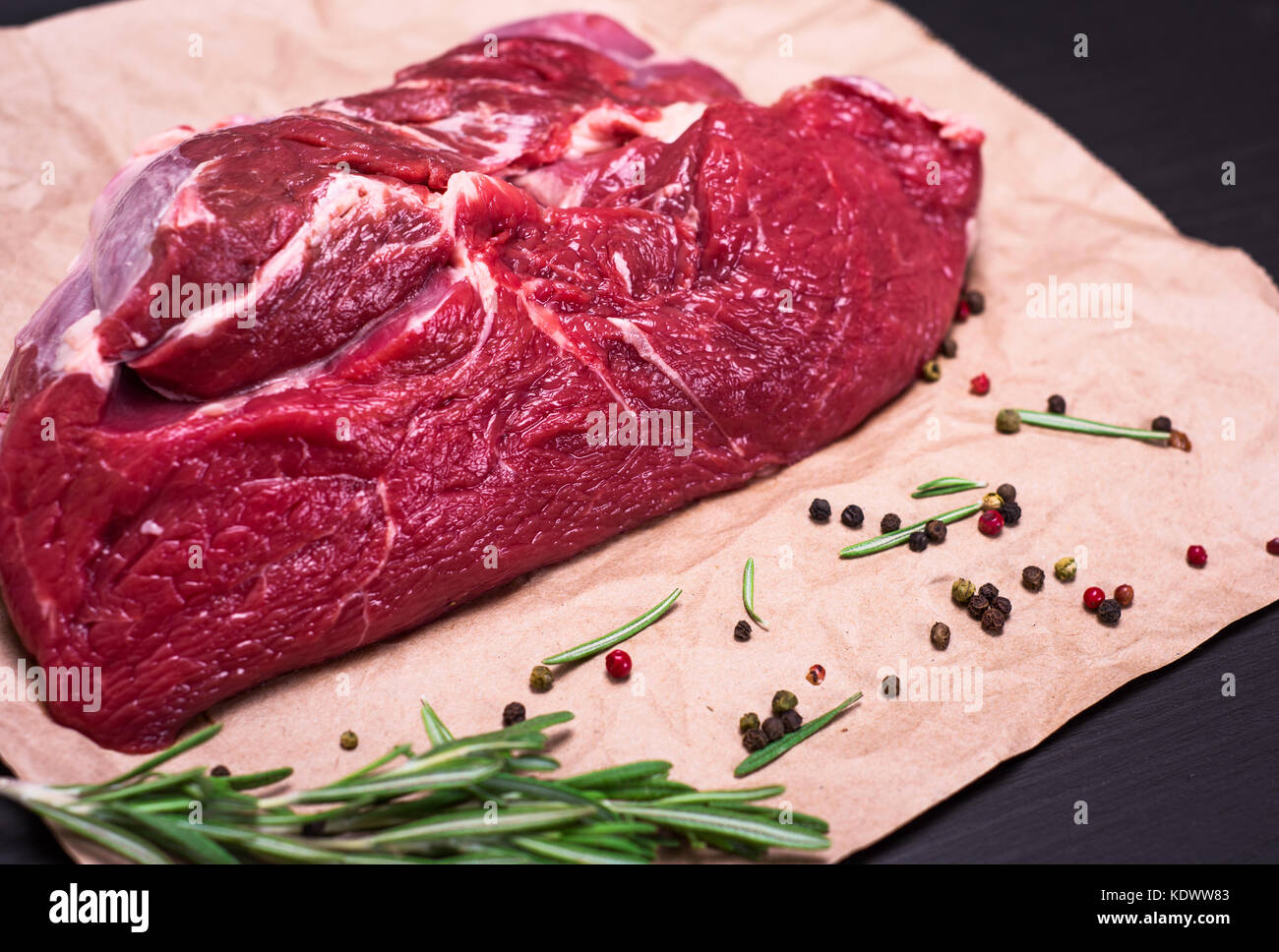 A fresh piece of beef on brown kraft paper with spices and a rosemary ...