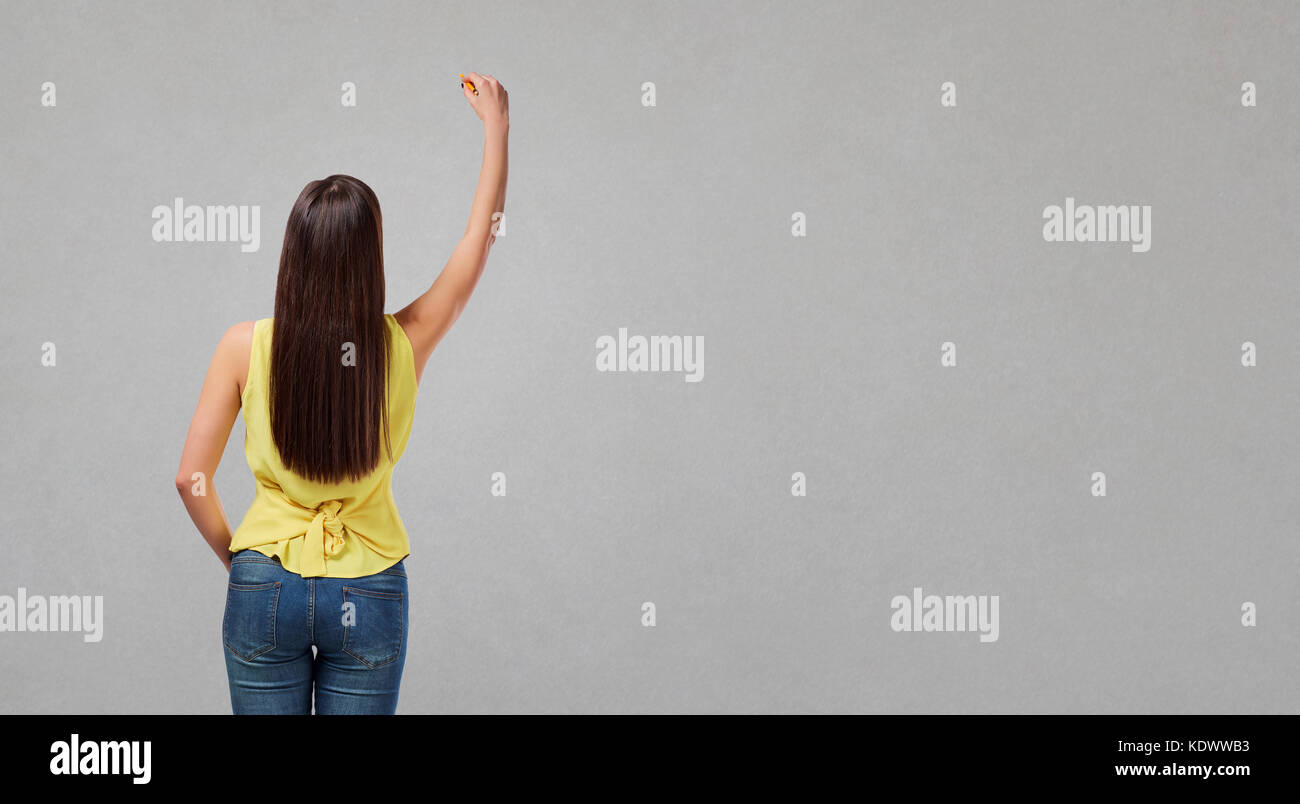 The girl is writing on the wall with a pencil. Back view Stock Photo ...