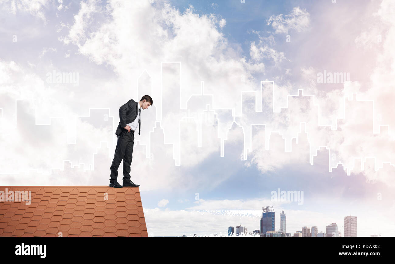 Businessman looking down from roof and modern cityscape at background ...