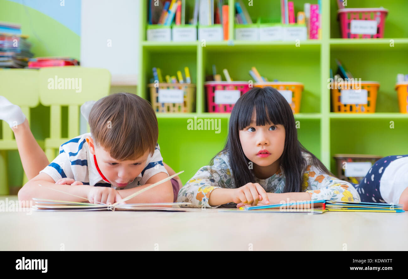 Two kid lay down on floor and reading tale book in preschool library ...