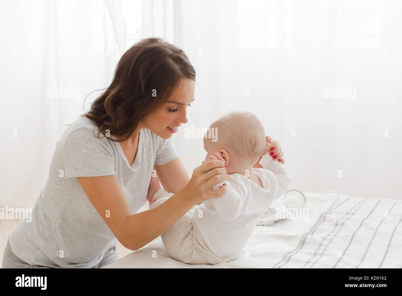 Mother helping child to sit on a white background Stock Photo - Alamy