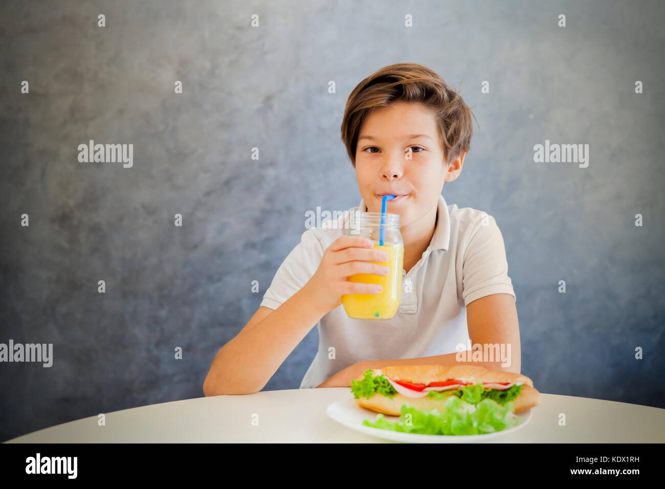 Portrait of cute teen boy drinking juice and eating sandwich at home ...