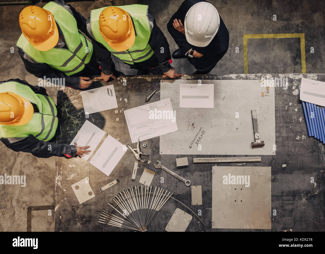 Workers and manager in safety helmets working with documents at factory ...