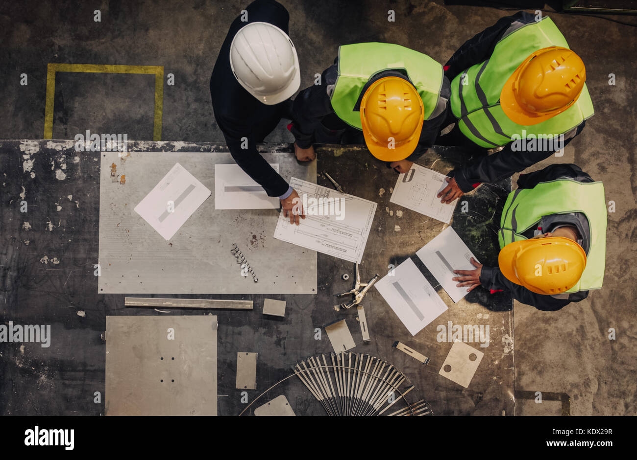 Workers and manager in safety helmets working with documents at factory ...