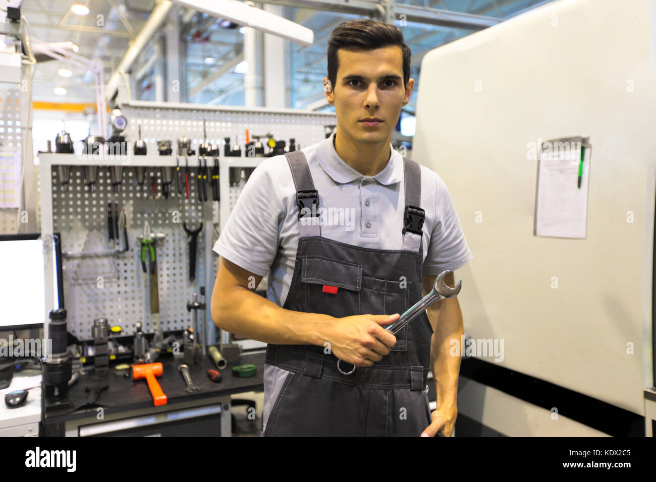 Portrait of a young worker holding wrench at workplace with computer ...