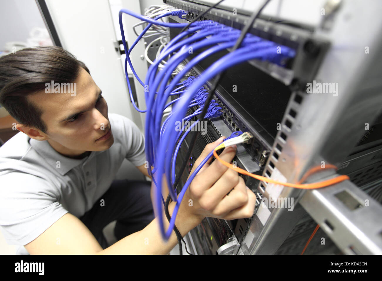 Young engeneer man in network server room connecting wires and checking ...
