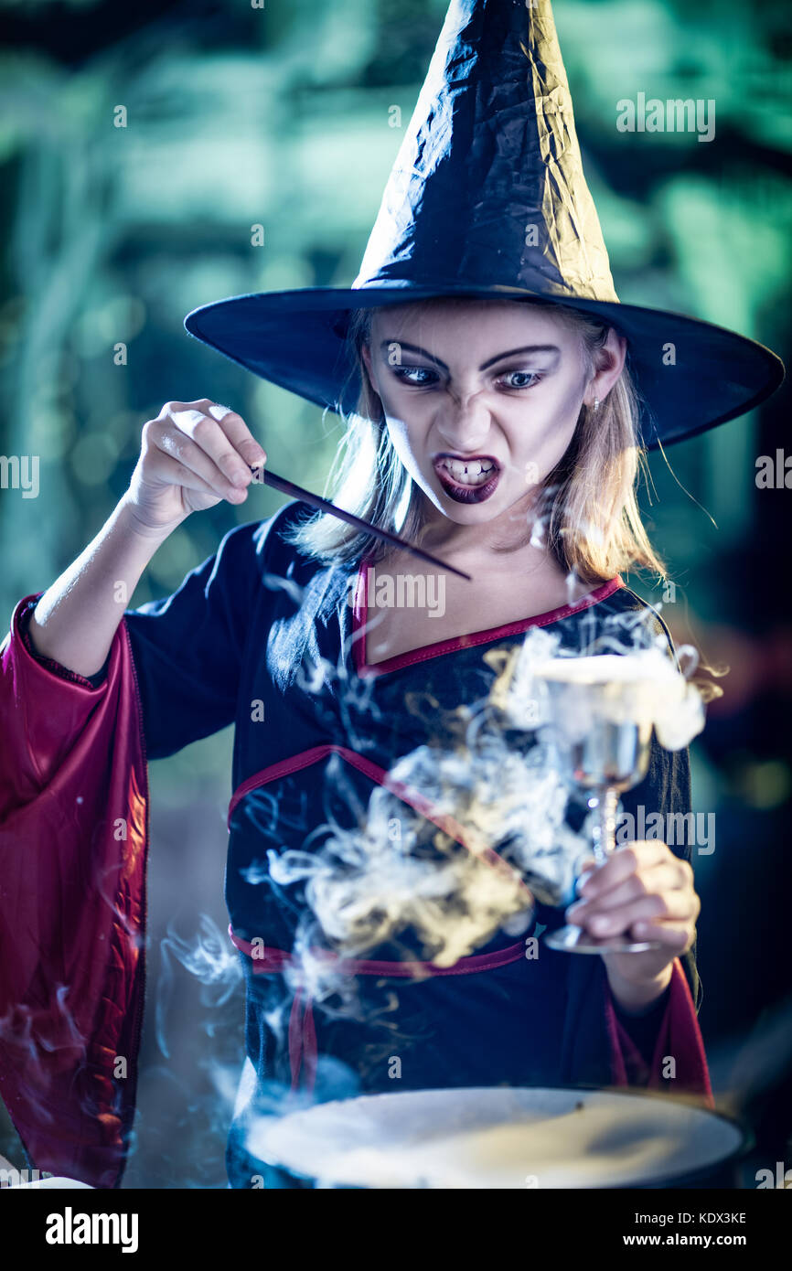Young witch with angry evil face holds a goblet with magic potion in ...