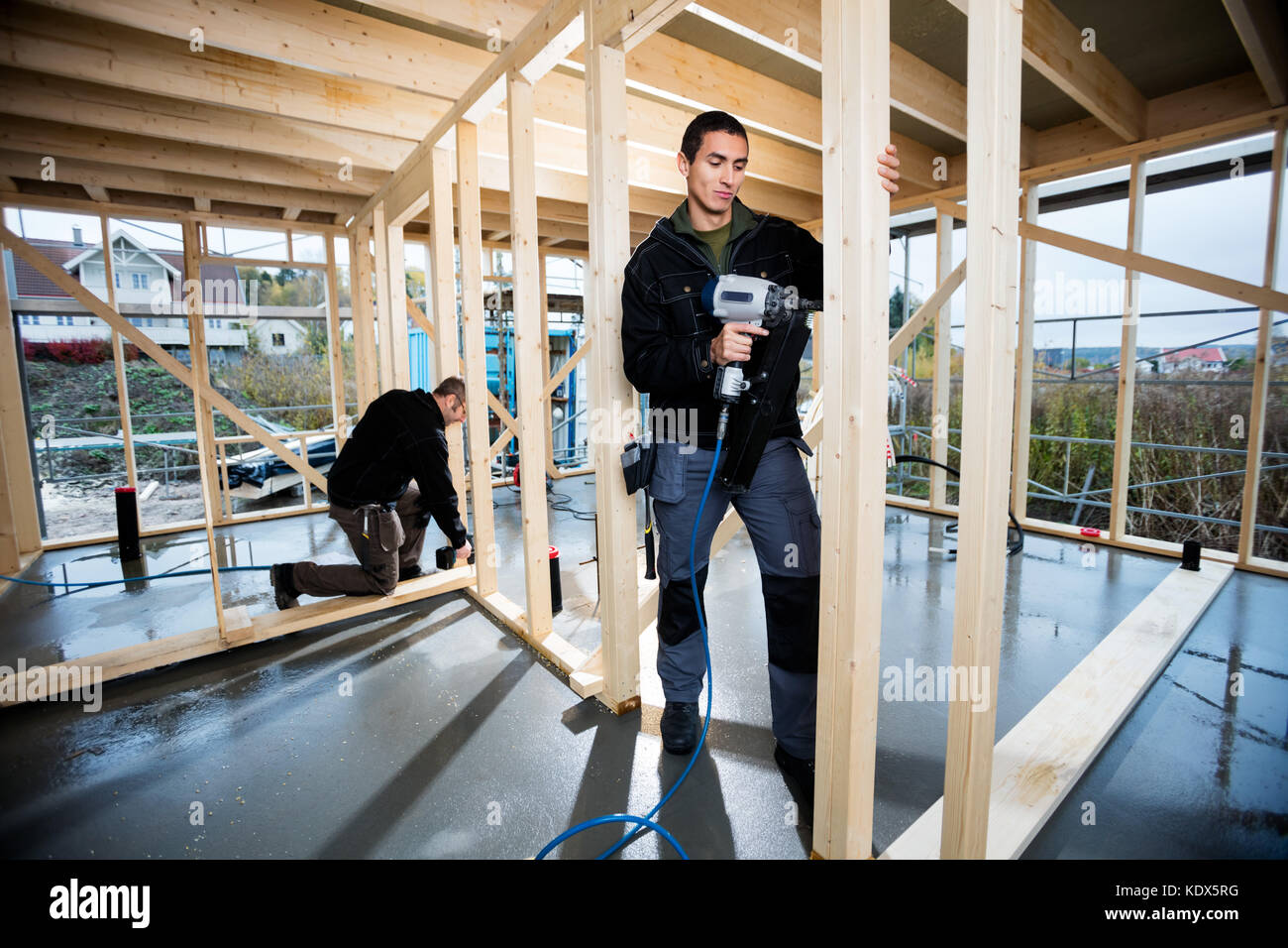 Full length portrait of carpenter drilling plank while colleague ...