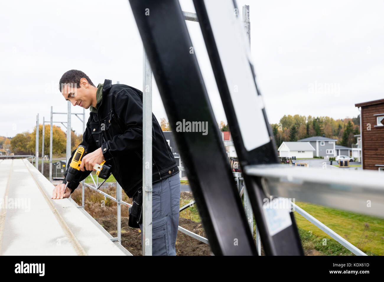 Confident young carpenter drilling wooden roof at construction site ...