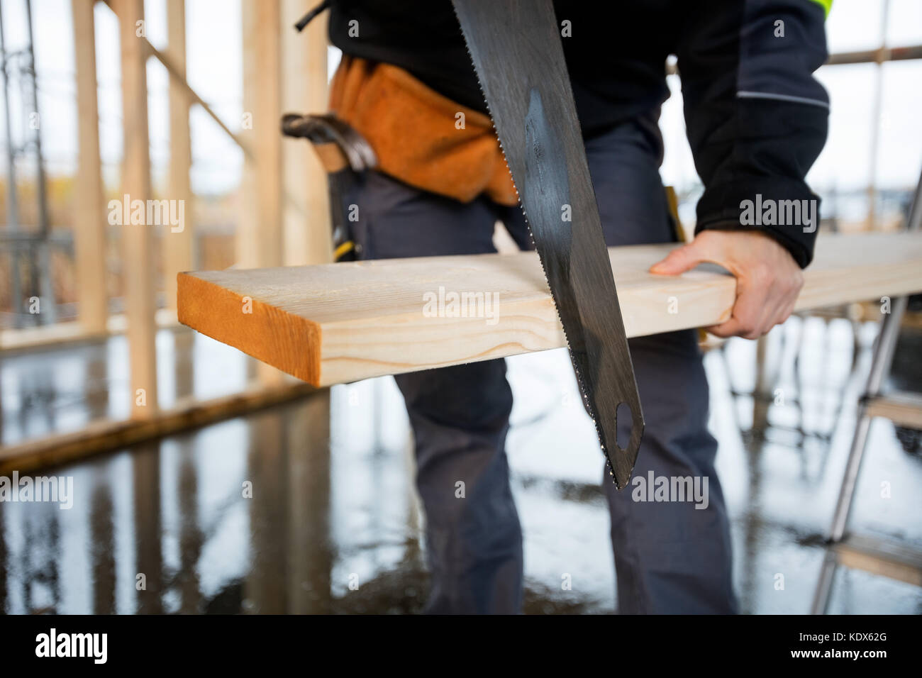 Midsection of female carpenter using hand saw to cut plank at site ...