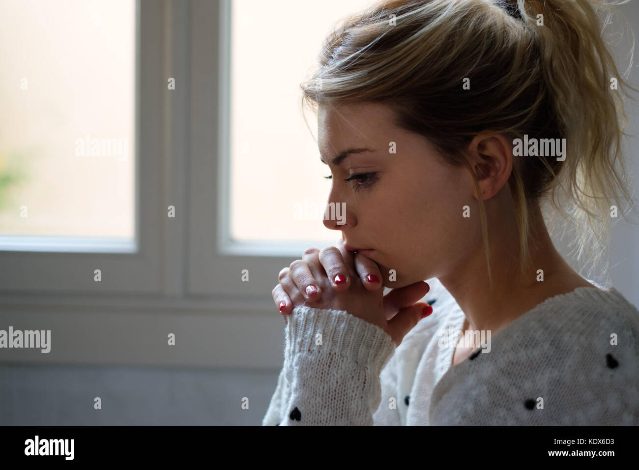 Hopeless young girl praying next to the window Stock Photo - Alamy