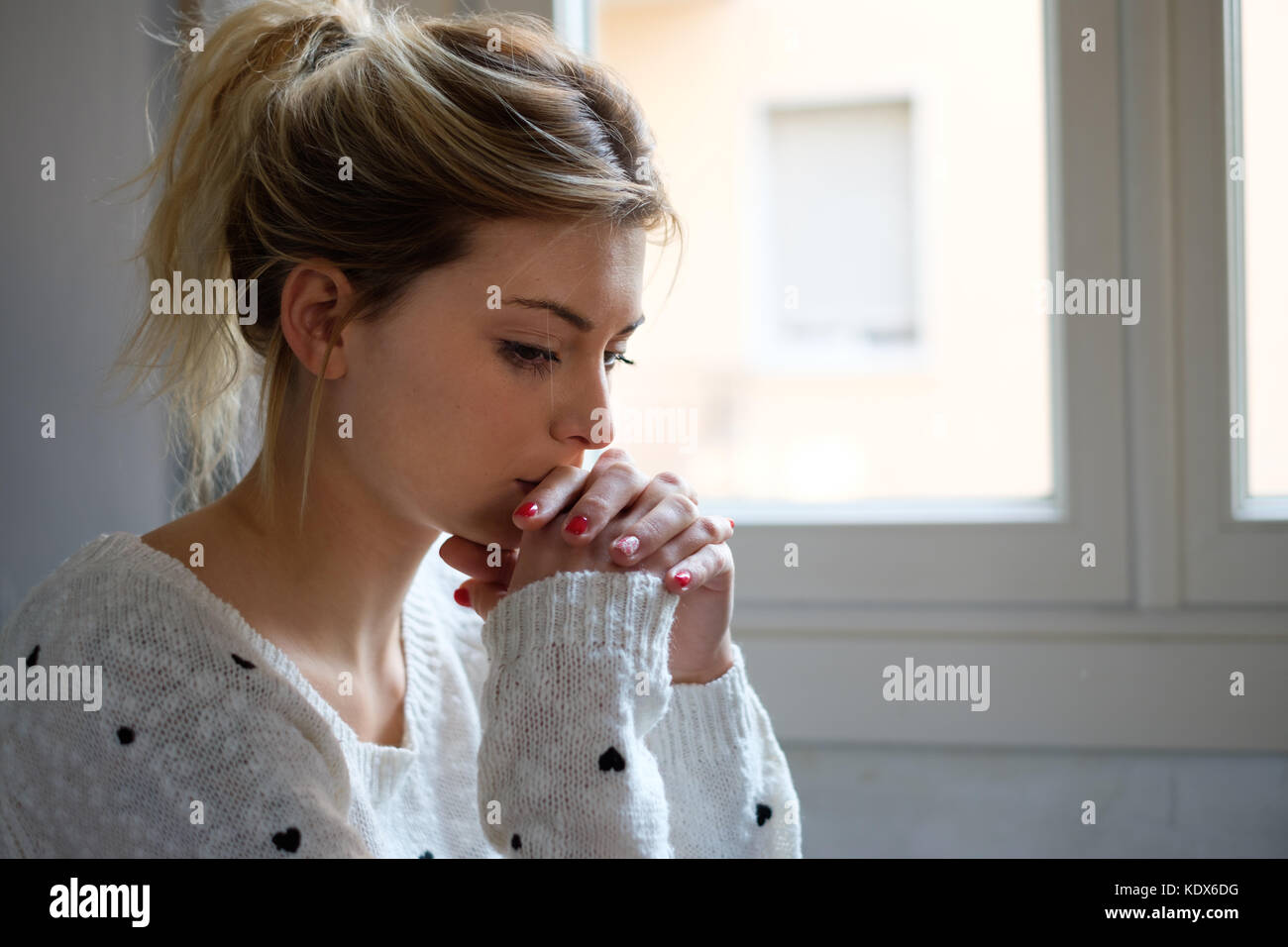 Hopeless young girl praying next to the window Stock Photo - Alamy