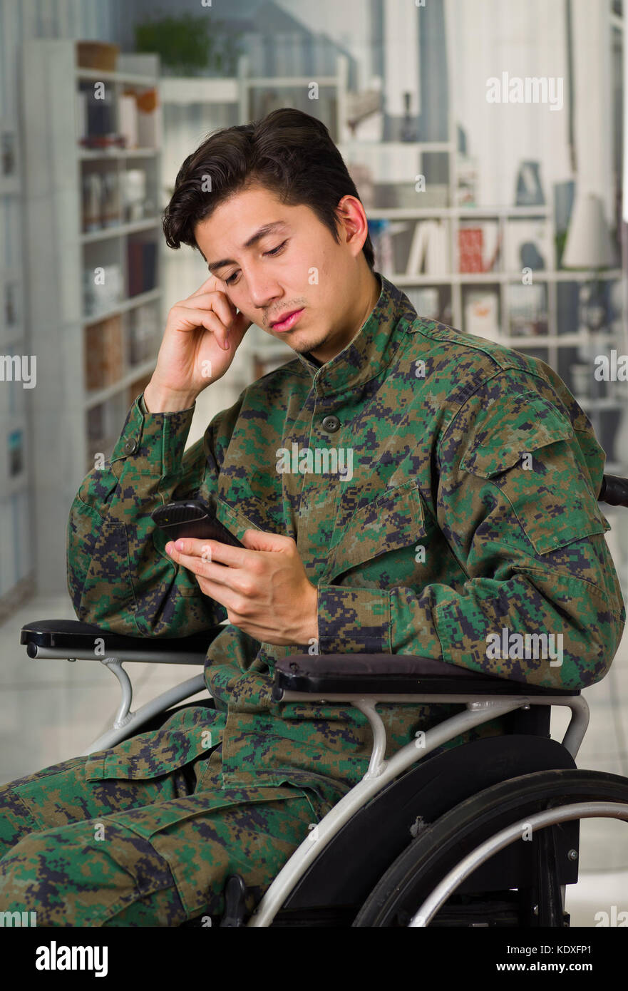 Close up of a thoughtful young soldier sitting on wheel chair using his ...