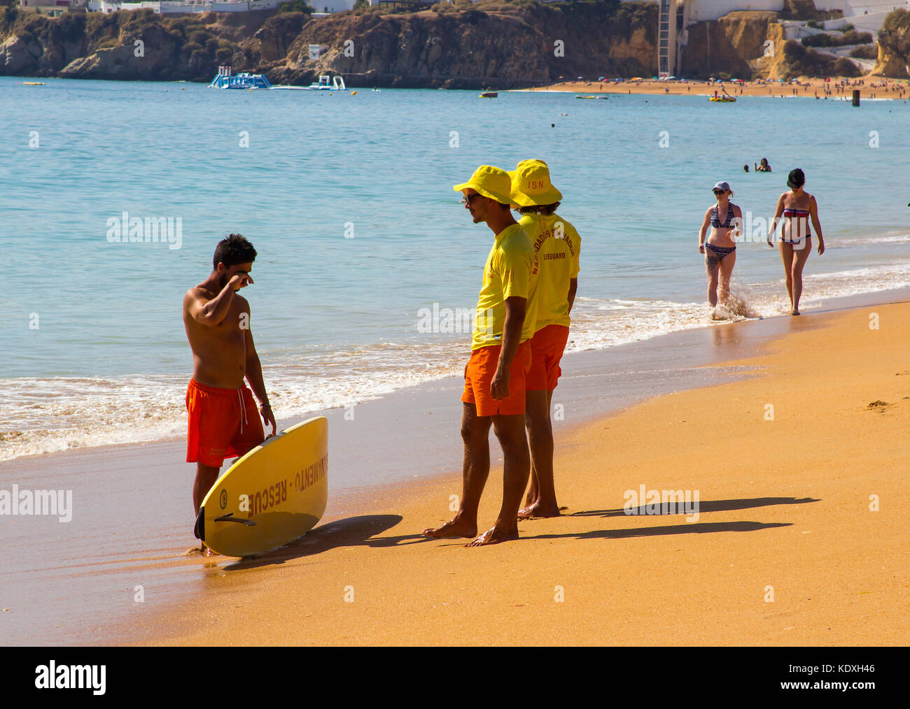 Two young lifeguards chat to a surfer at the waters edge on the beach ...