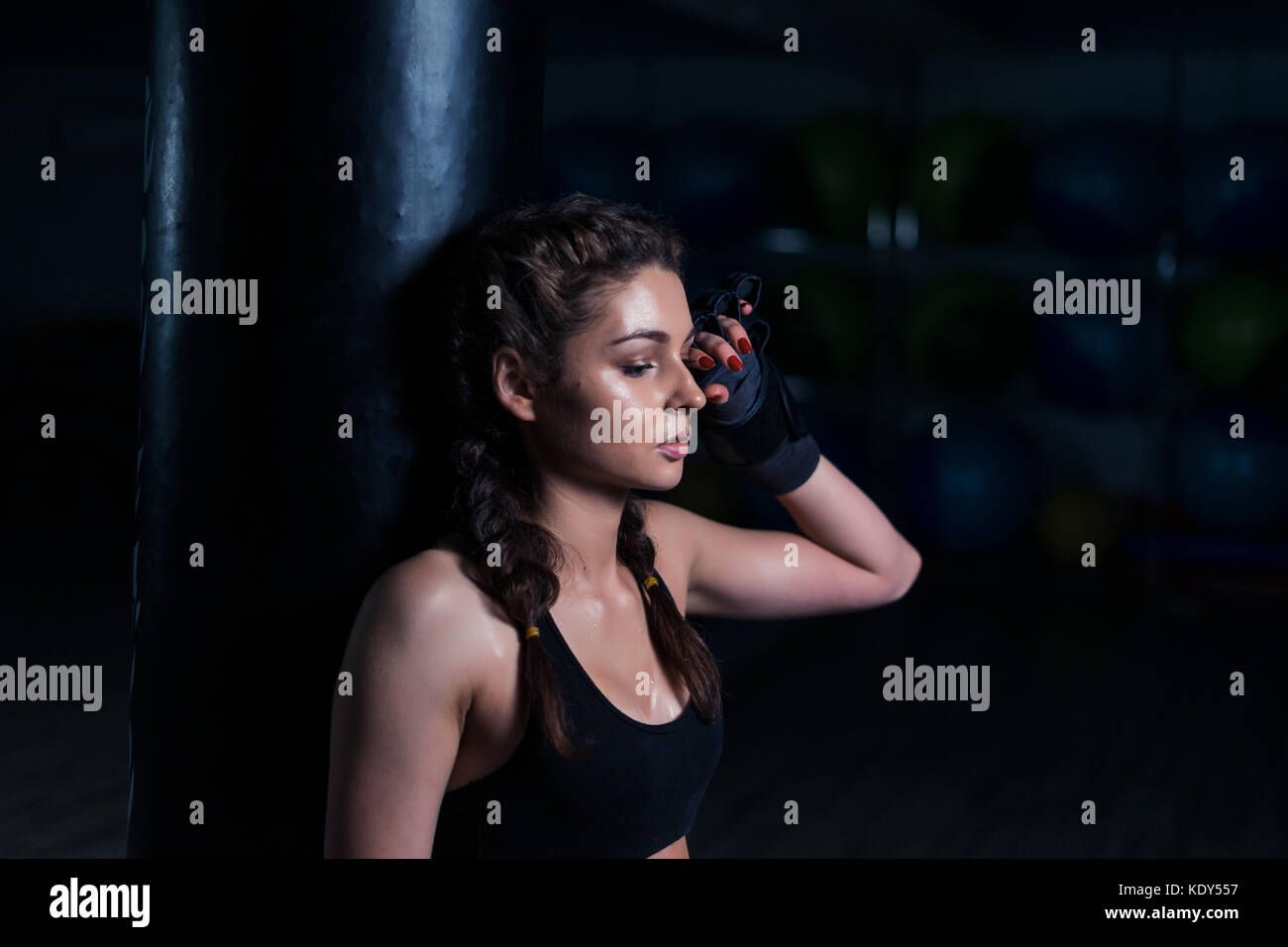 Upset young fighter boxer girl wearing boxing gloves, standing in dark ...