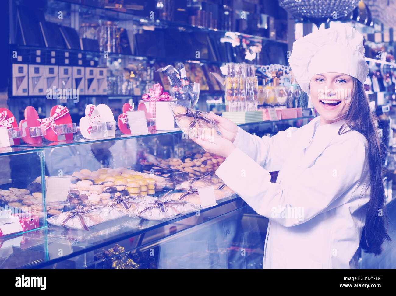 Cheerful young shopgirl posing with different chocolate and ...