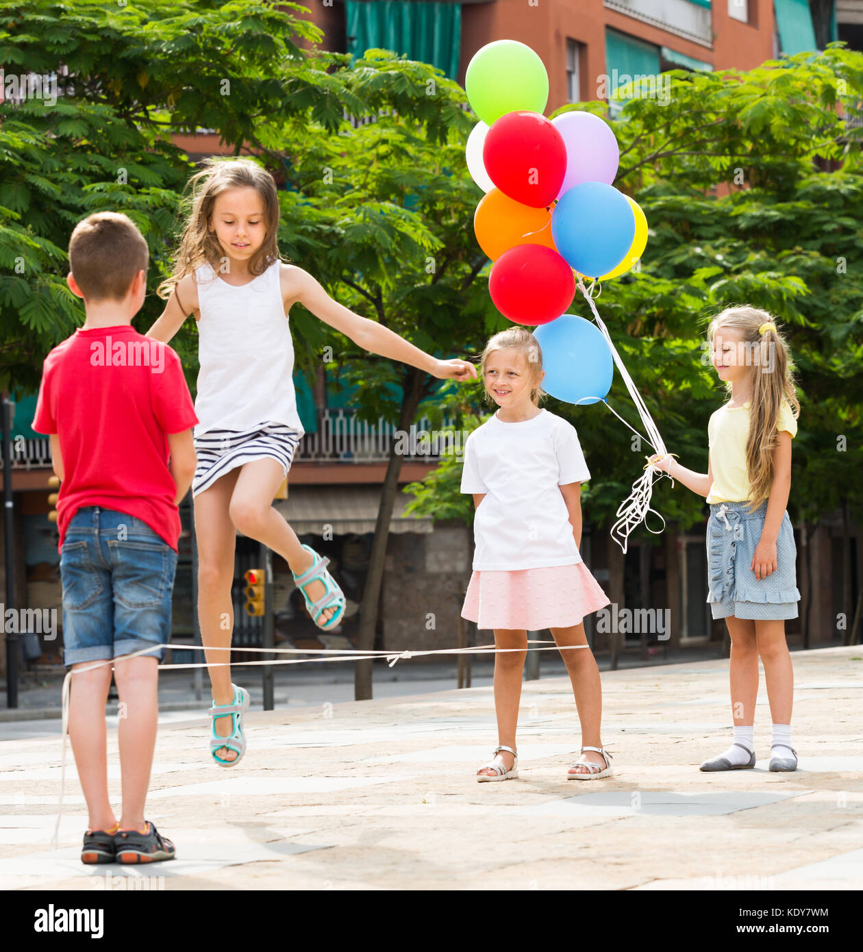 Cheerful kids in school age playing together with chinese jumping rope ...