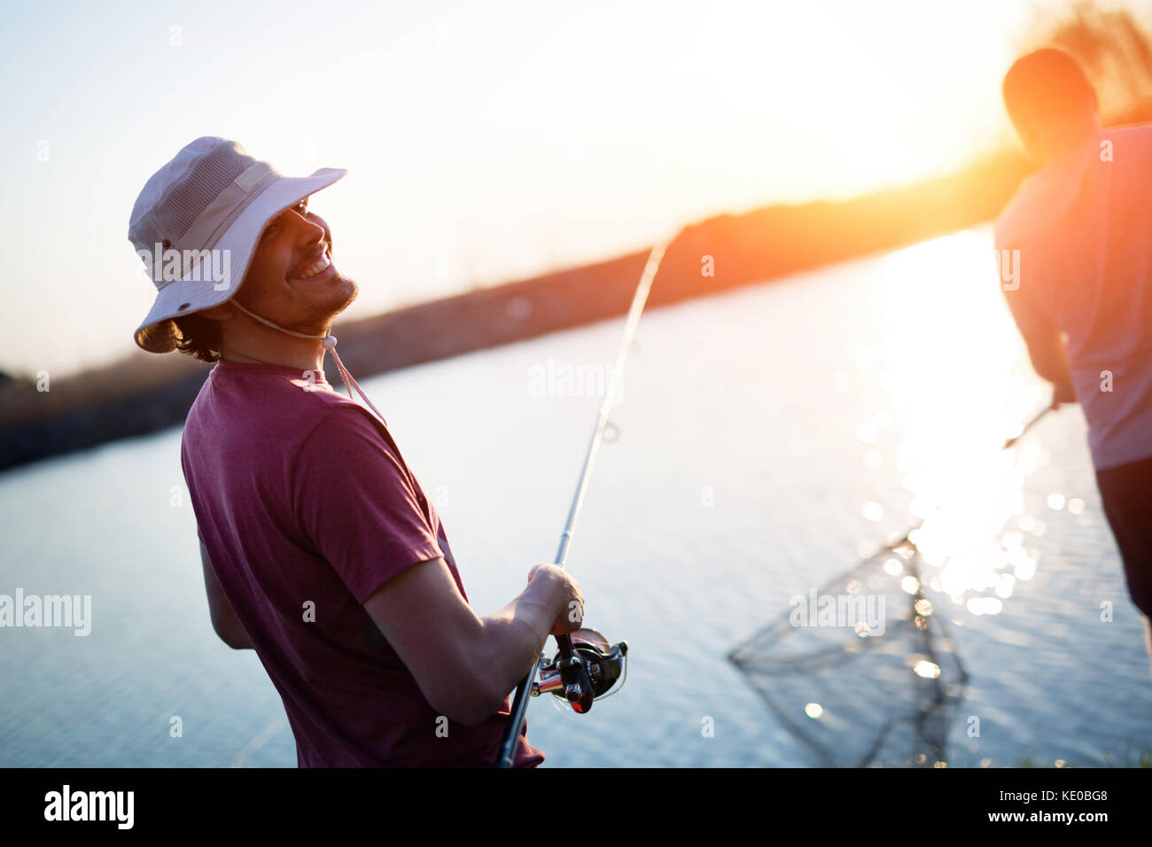 Young man fishing on a lake at sunset and enjoying hobby Stock Photo ...