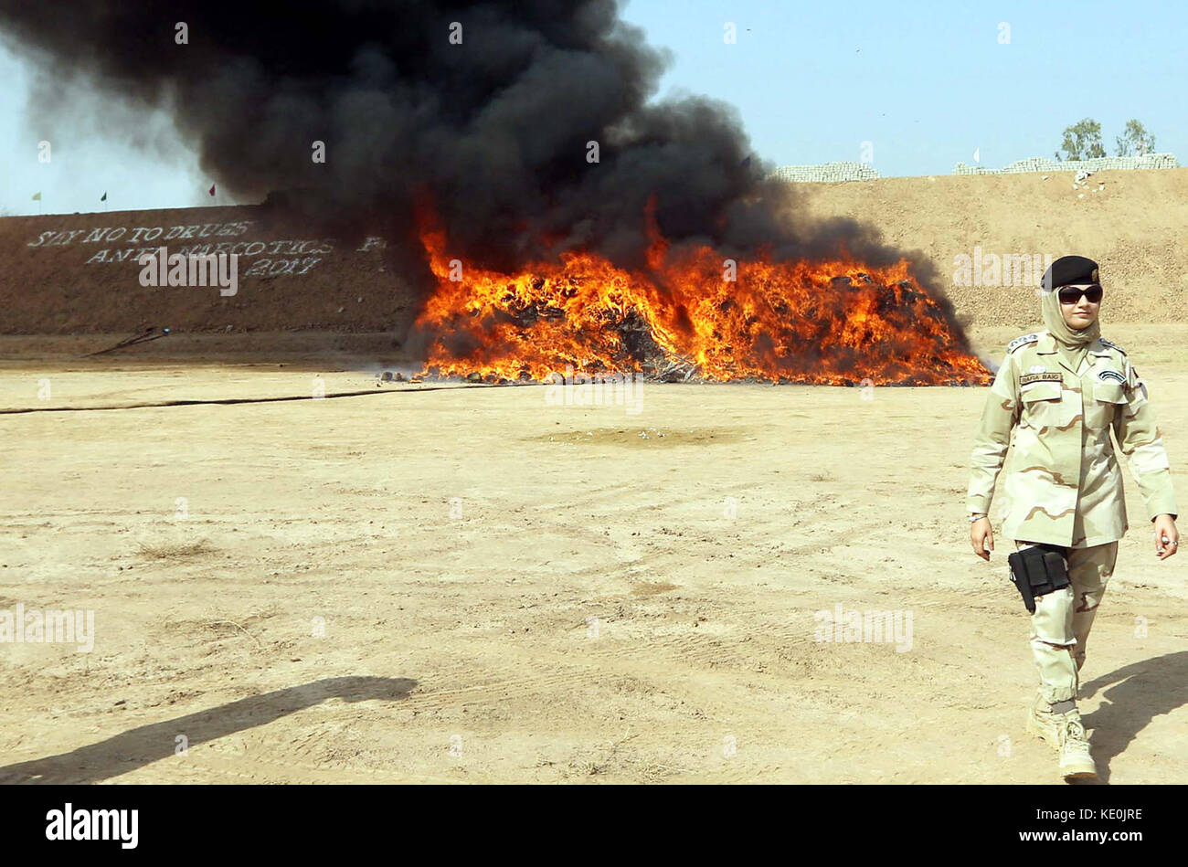 Anti-Narcotics Force (ANF) officials stand alert near burning pile of ...