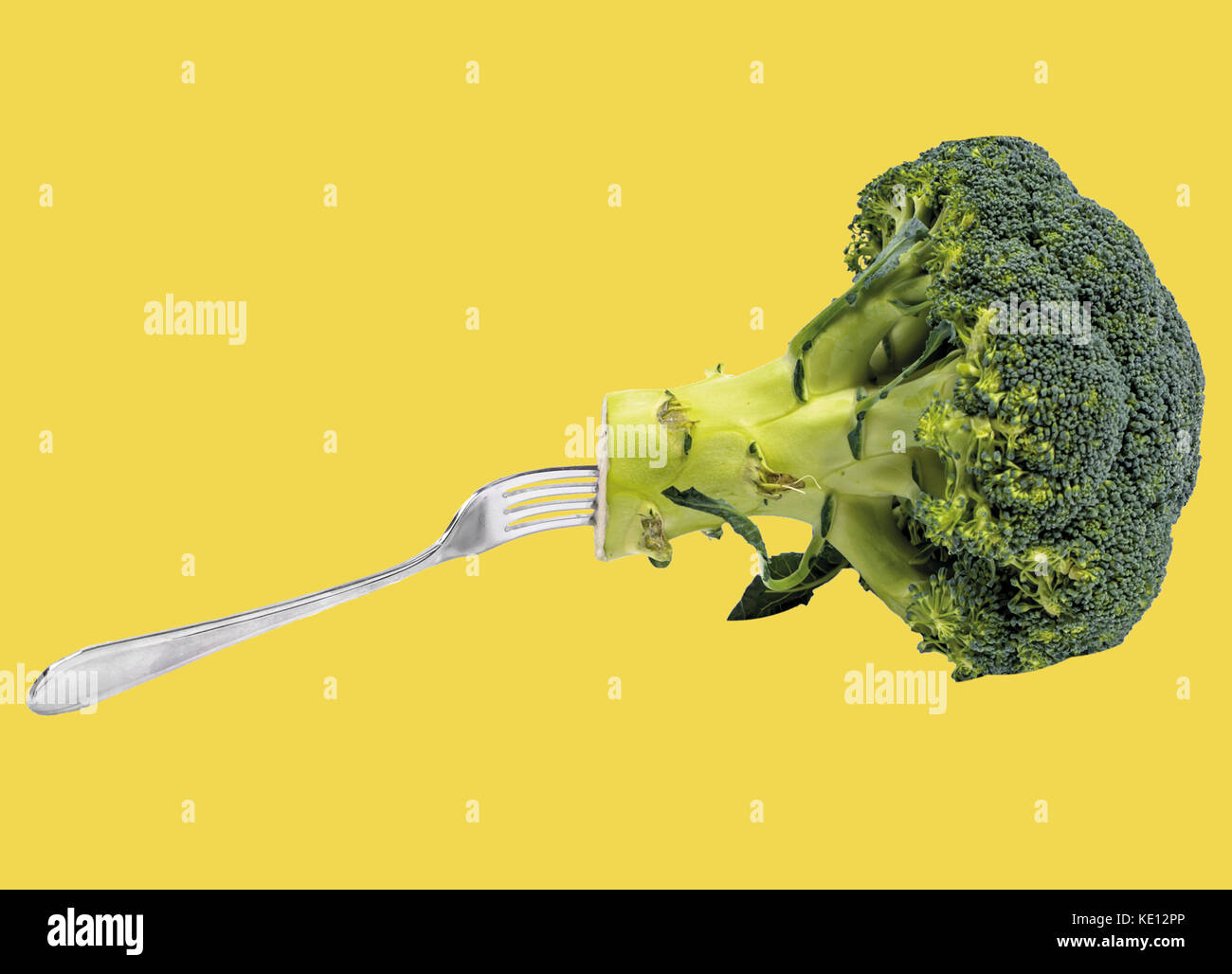 Fork stuck in broccoli on a yellow background Stock Photo - Alamy