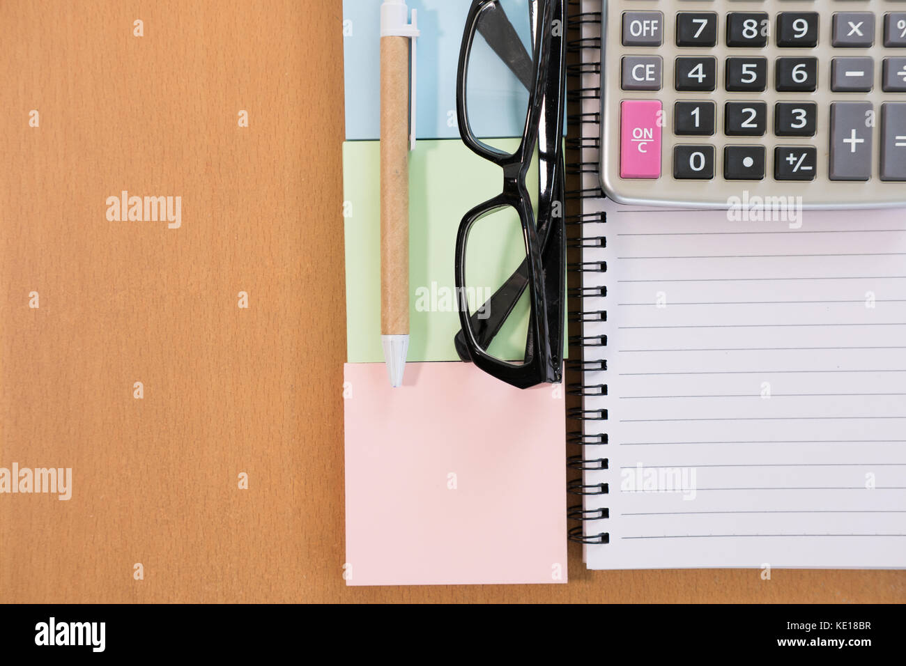 sticky note, calculator, ballpoint pen, empty notebook, eyeglasses on ...