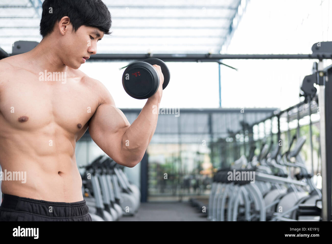 young man lift dumbbell in gym. bodybuilder male working out in fitness ...