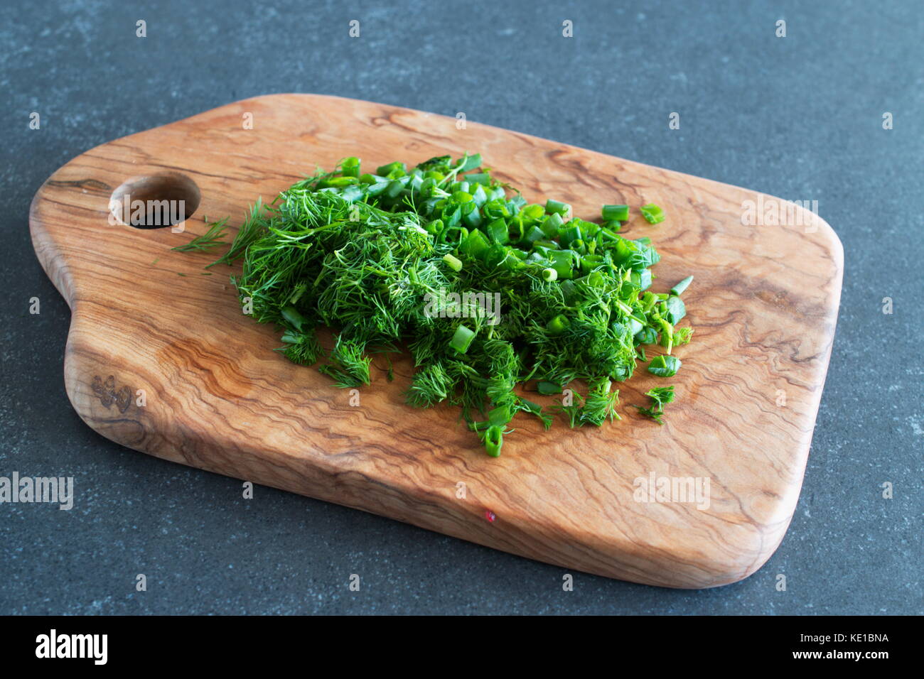 Cut fresh green onions and dill on olive wooden cvuttingboard Stock ...