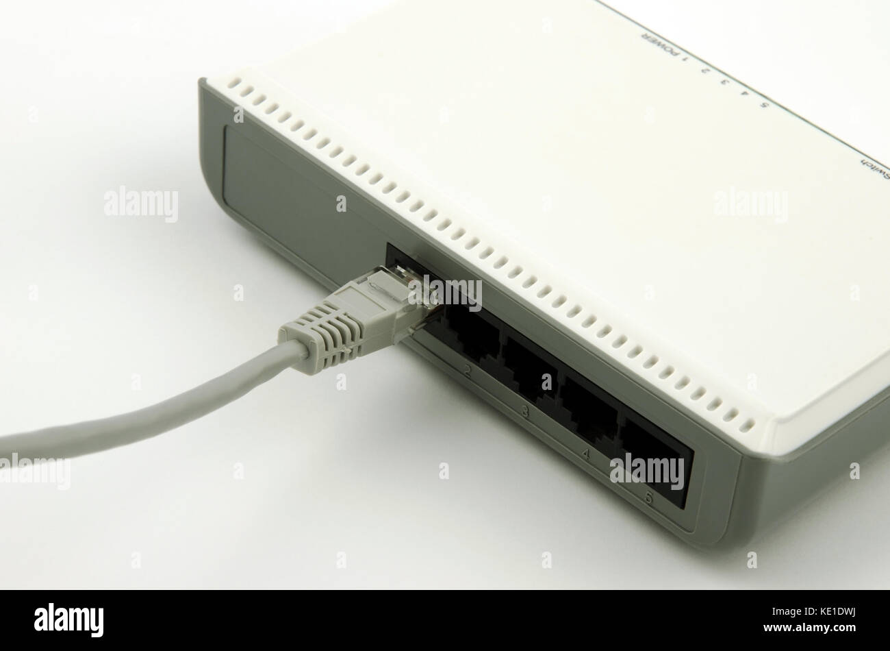 Close-up view of a gray lan cable plugged into a router with empty slots on a white background ...