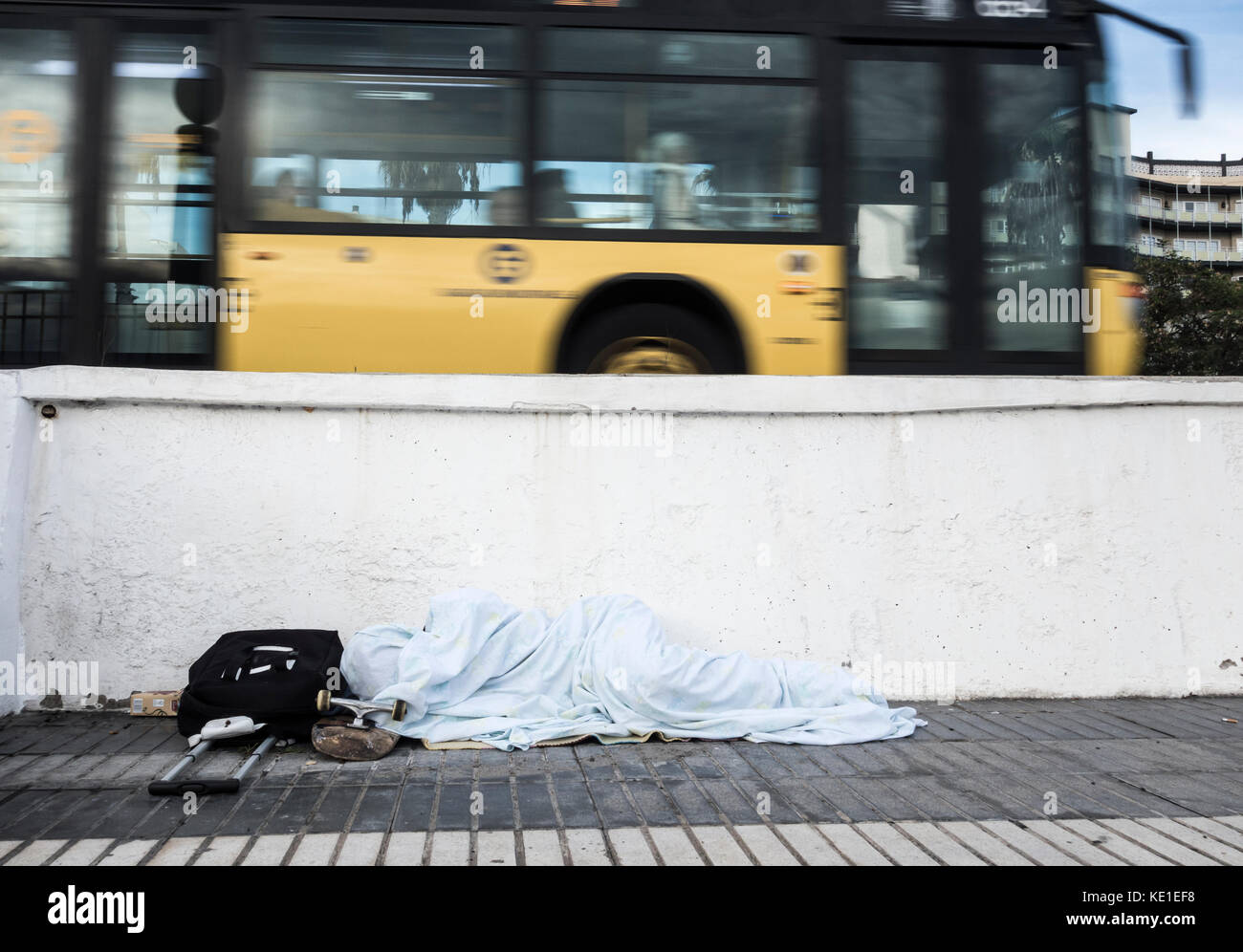 homeless person with skateboard and wheeled suitcase sleeping near busy ...