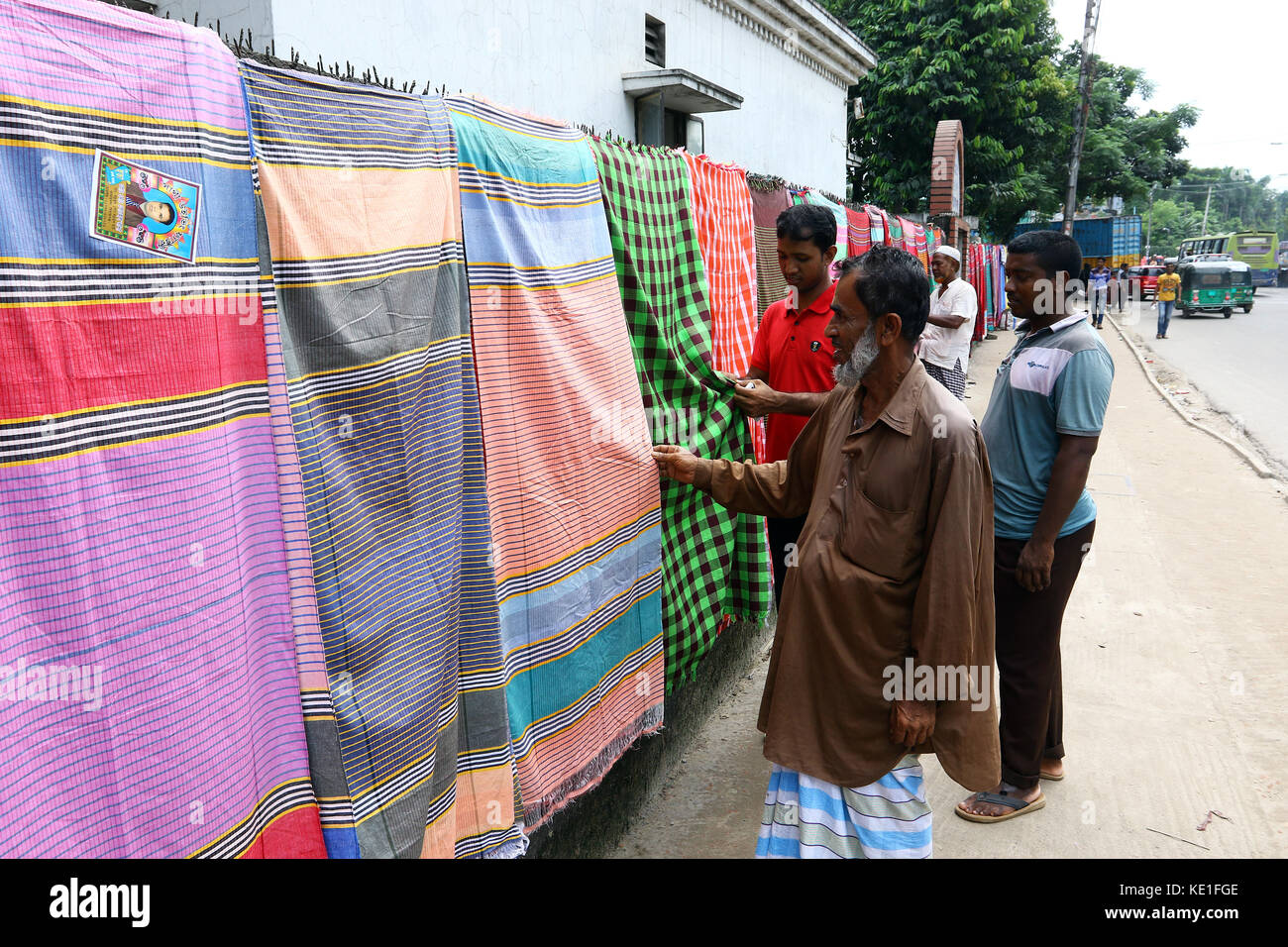 A Bangladeshi vendor sits under his display of traditional towels or ...