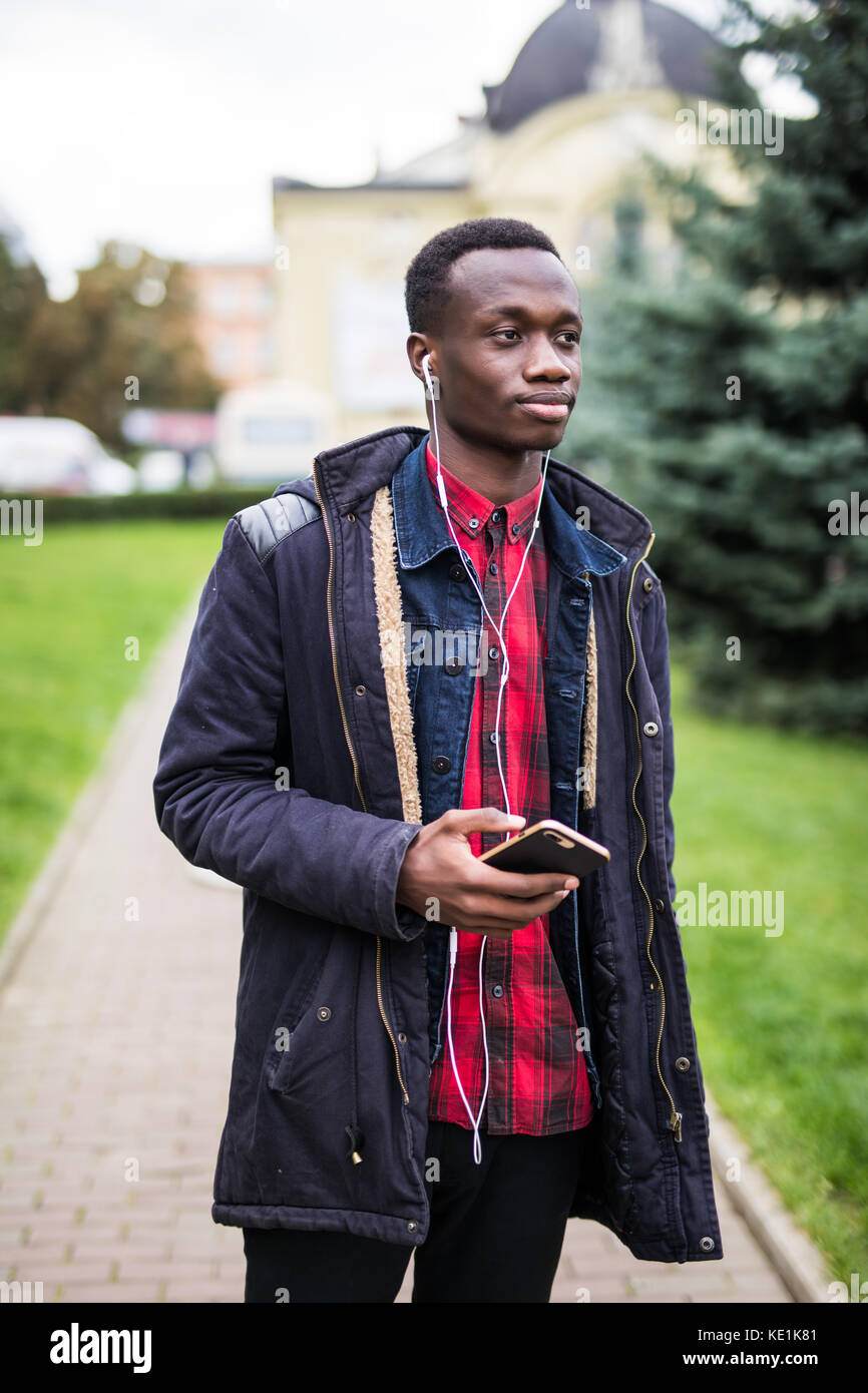 Young african man listening music in big headphones. Student relaxing, dreaming holding smart ...