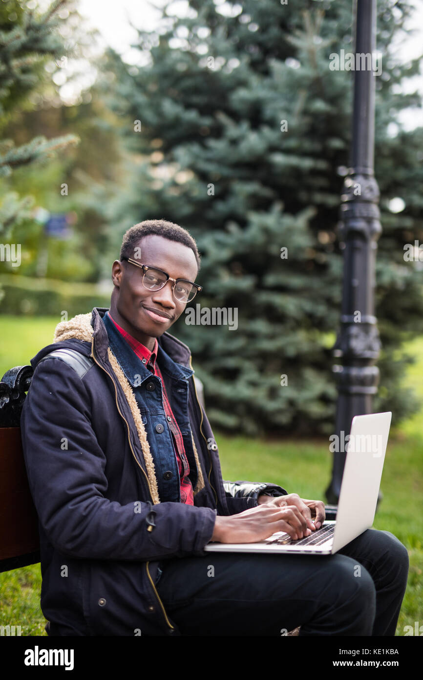 Joyful African man using computer outdoors on the bench Stock Photo - Alamy